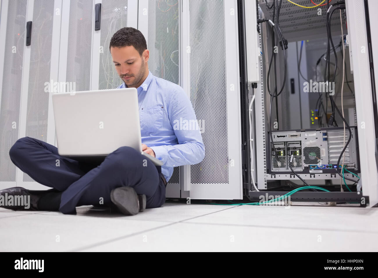 Man sitting on floor with laptop beside servers in data center Stock ...