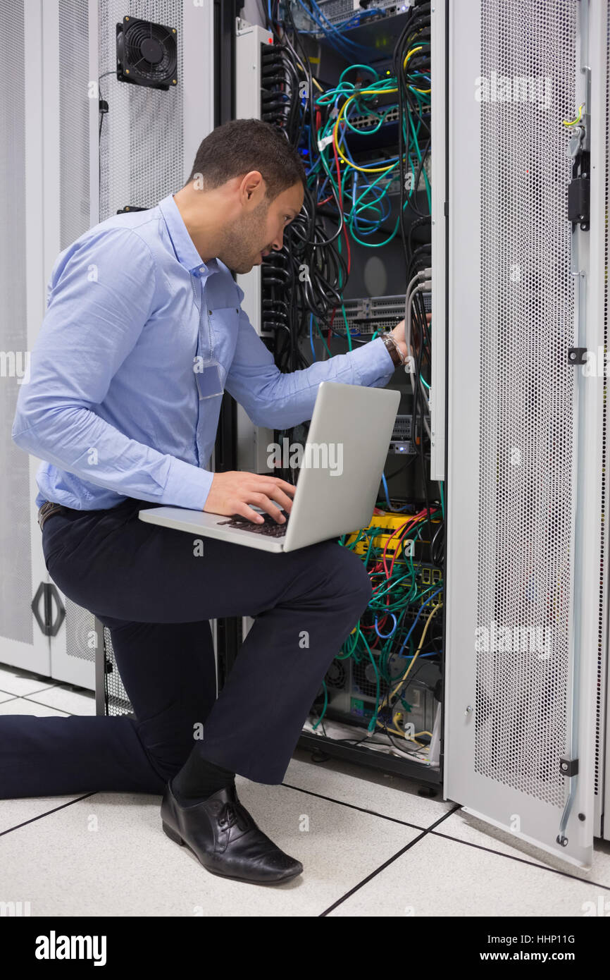 Man fixing wires while doing maintenance with laptop in data center ...