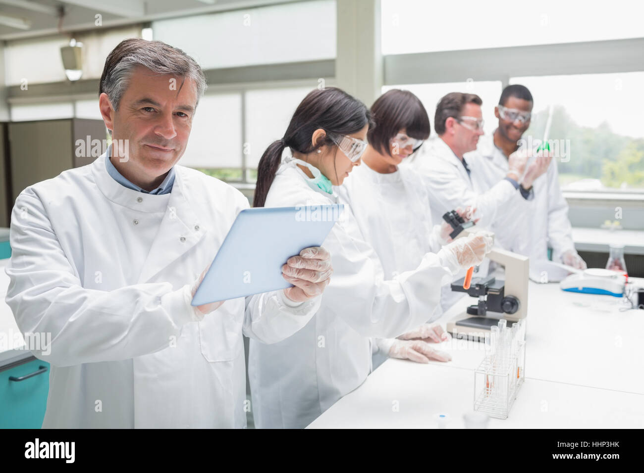 Smiling chemist using tablet pc in busy lab Stock Photo - Alamy