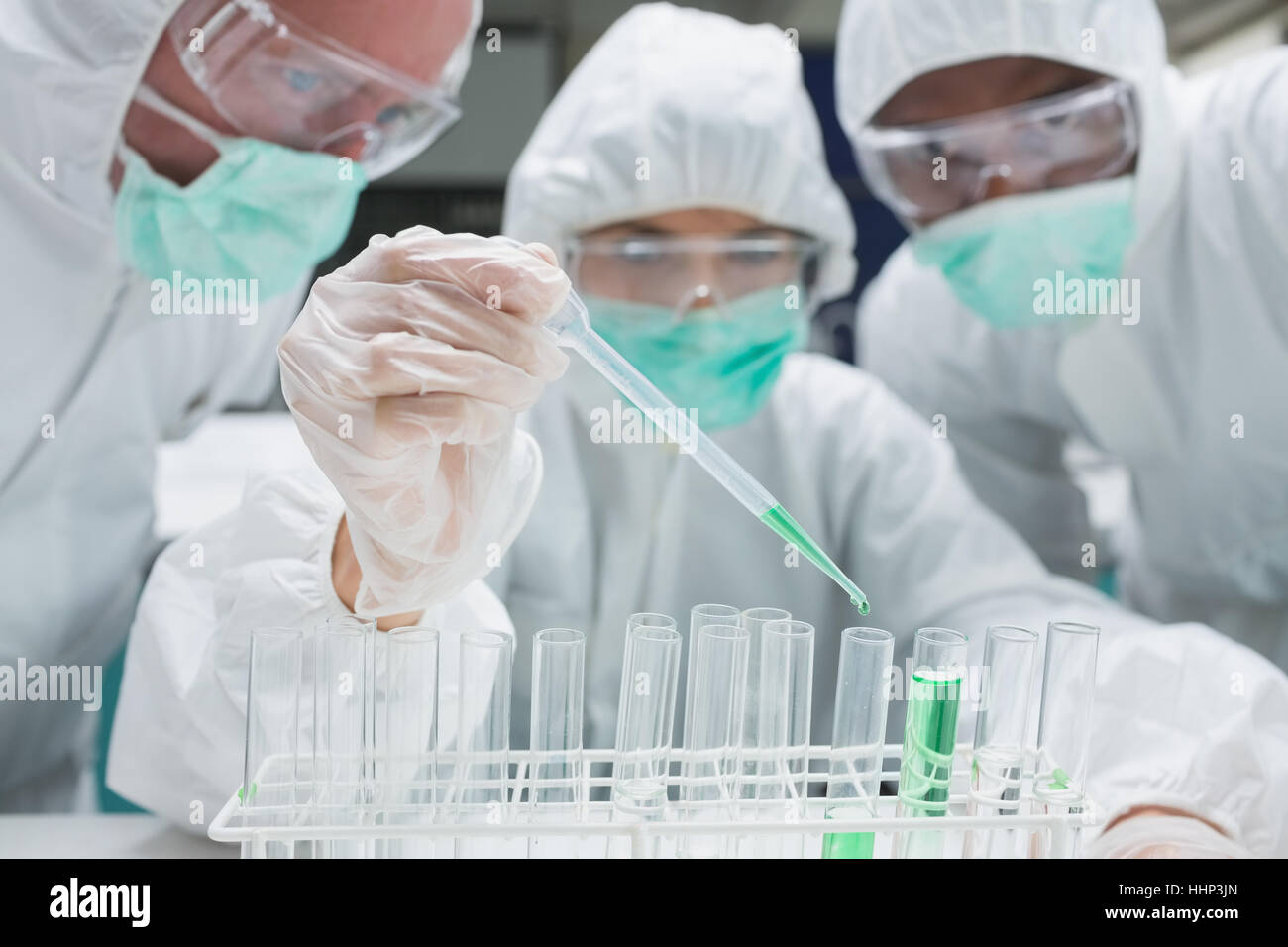 Chemist adding green liquid to test tubes as two others are watching in ...