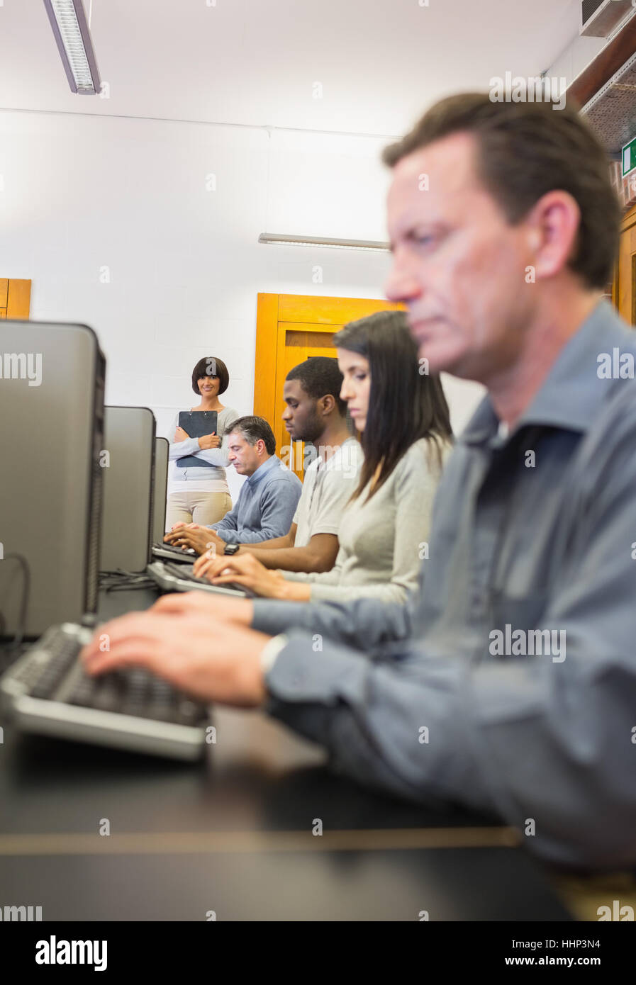 Teacher smiling while others working in computer class Stock Photo - Alamy