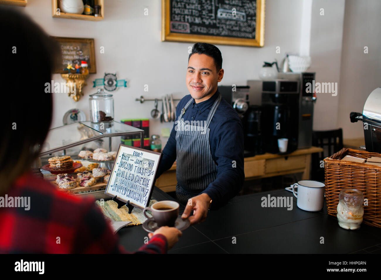 Hispanic barista servicing a customer some coffee at a coffee shop ...