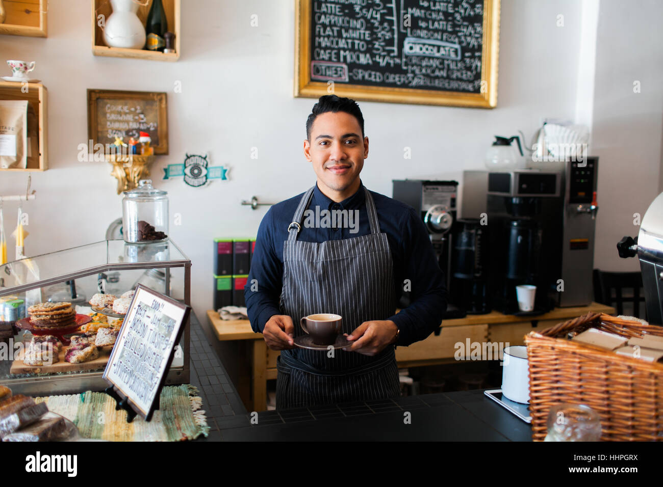 Happy latino man working in a coffee shop holding a customer's order ...