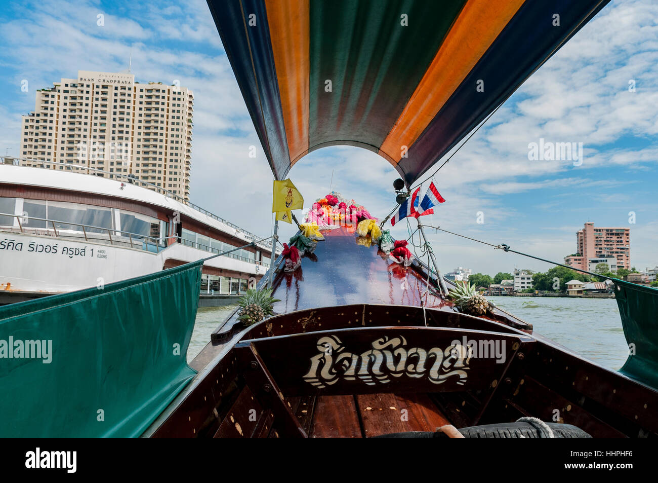 An open-air motorized boat headed down the Chao Phraya River in Bangkok ...