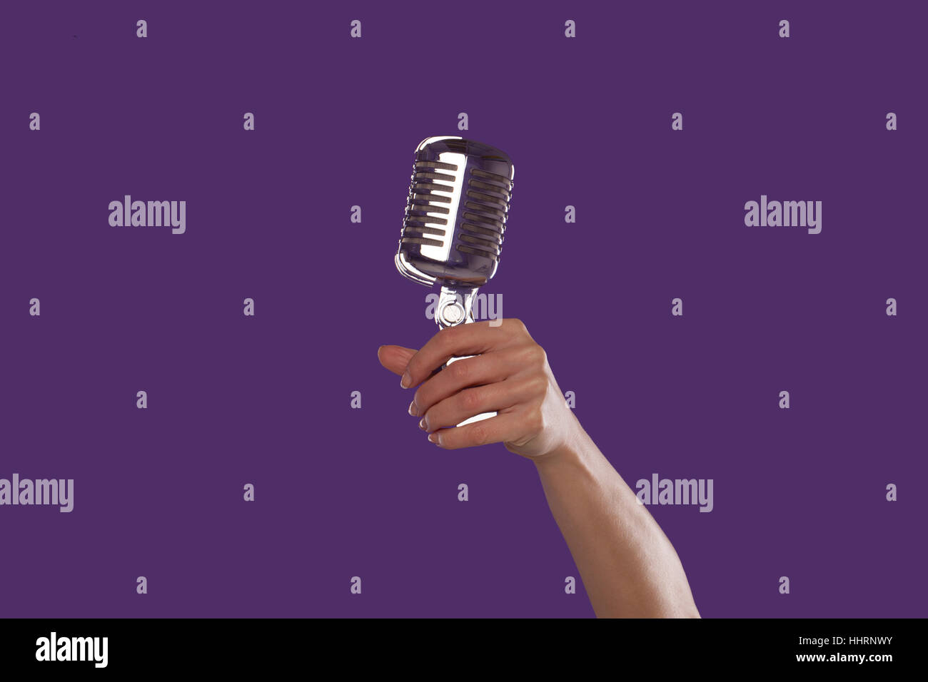 Female hand holding up a microphone over a purple studio background ...