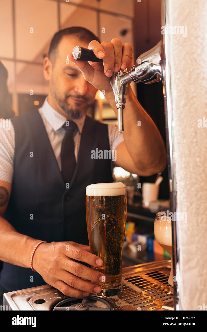 Barman hand at beer tap pouring a draught lager beer serving in a pub ...