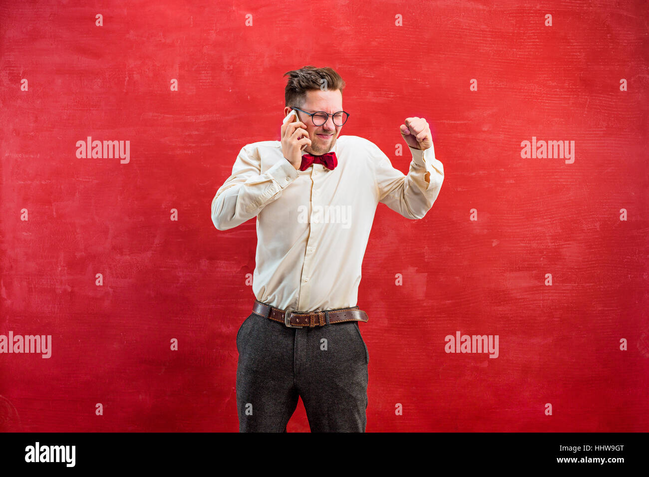 Portrait of puzzled man in glasses talking by phone on a red studio ...