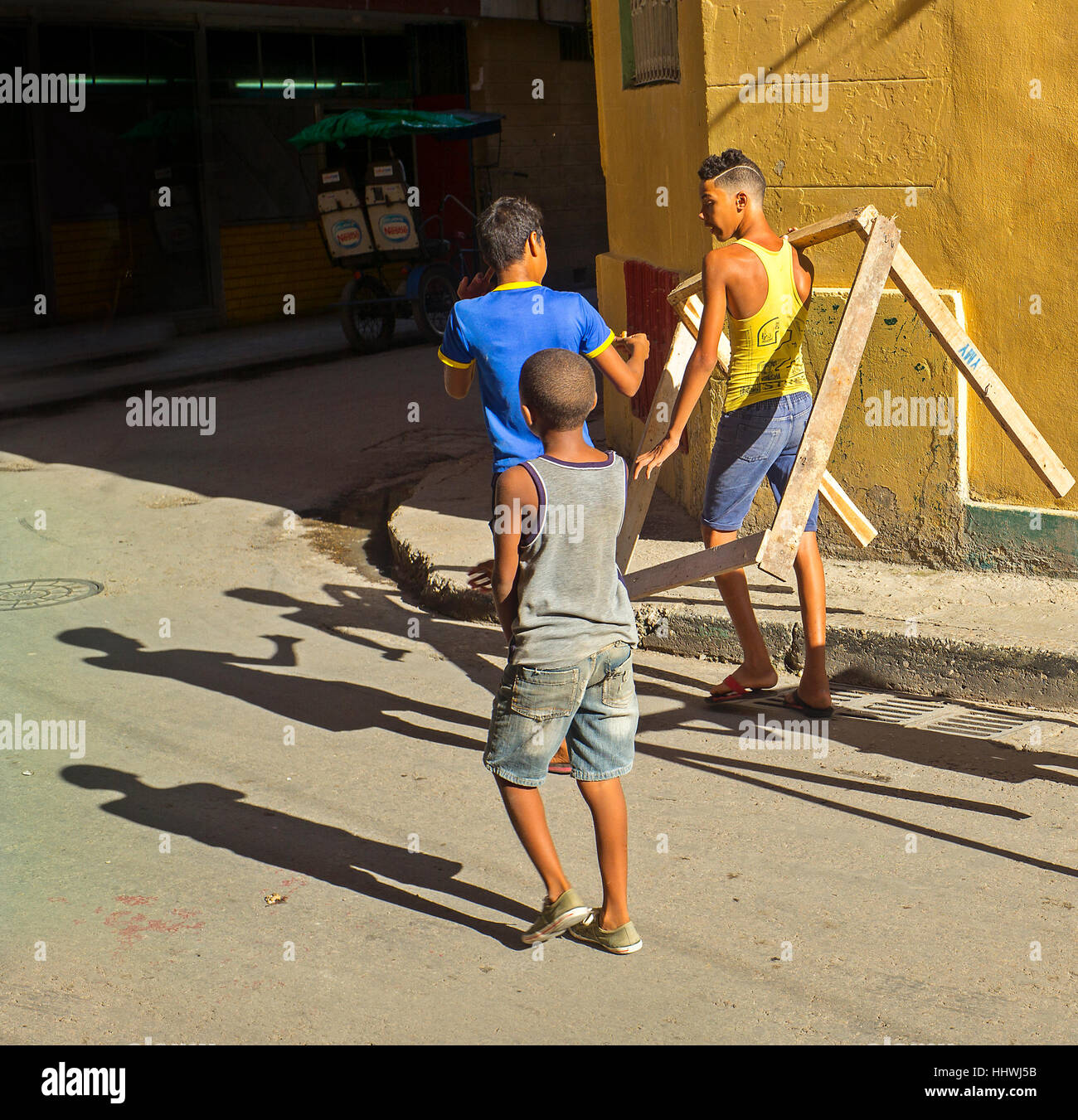 Boys carrying market stall supports legs through Havana street in sun ...