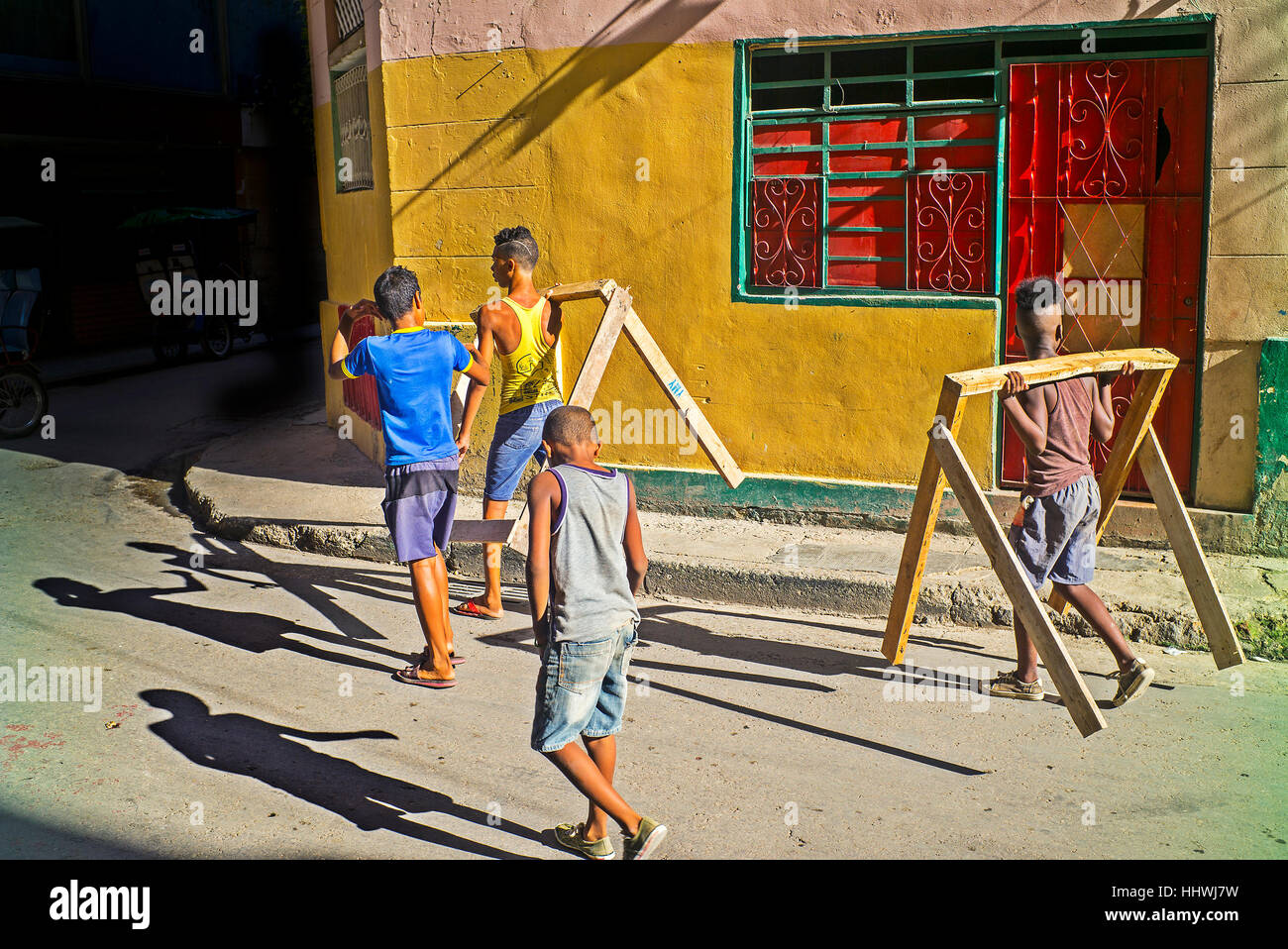 Boys carrying market stall supports legs through Havana street in sun ...