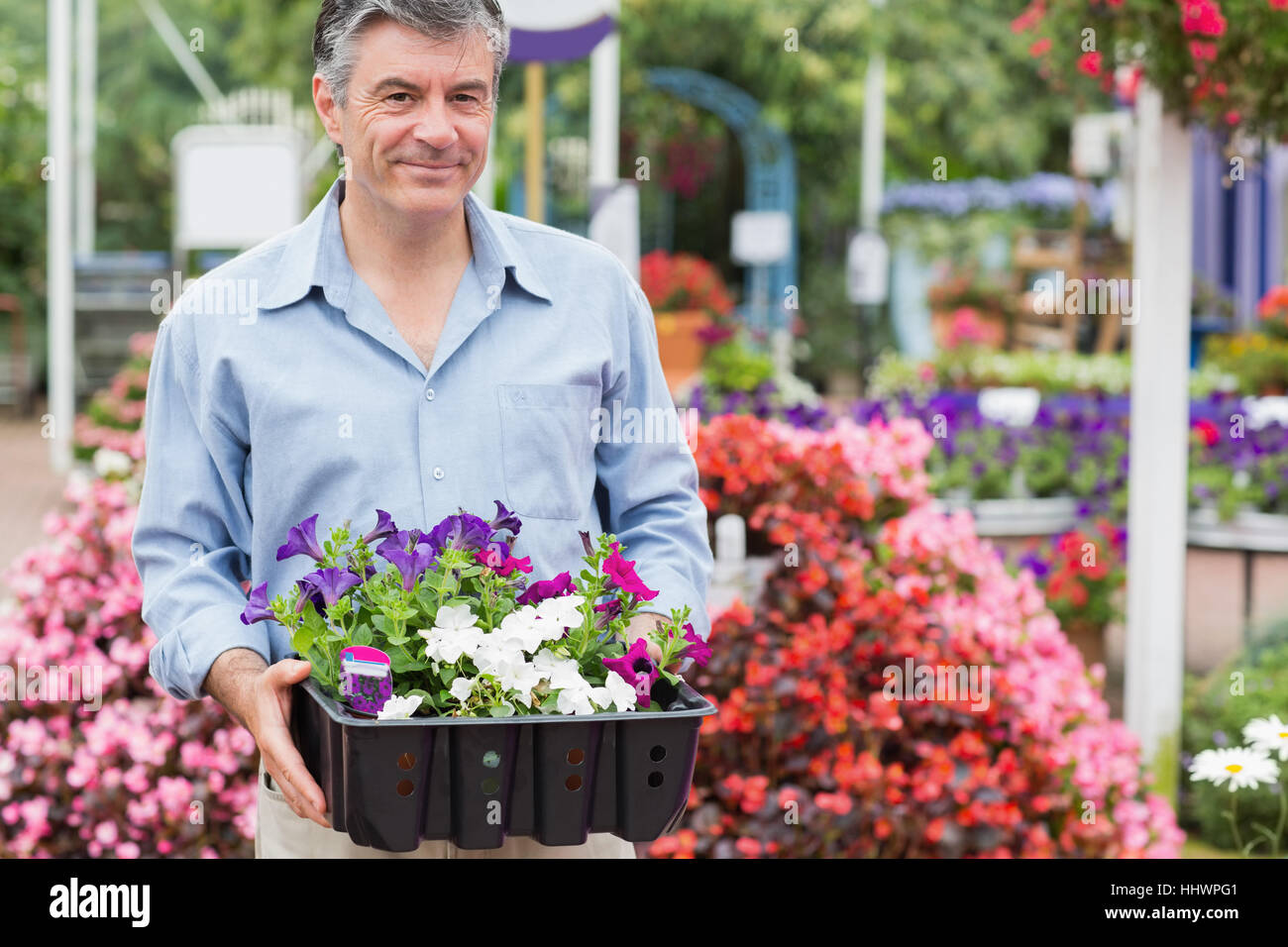 Man carrying boxes of flowers outside in garden center Stock Photo - Alamy