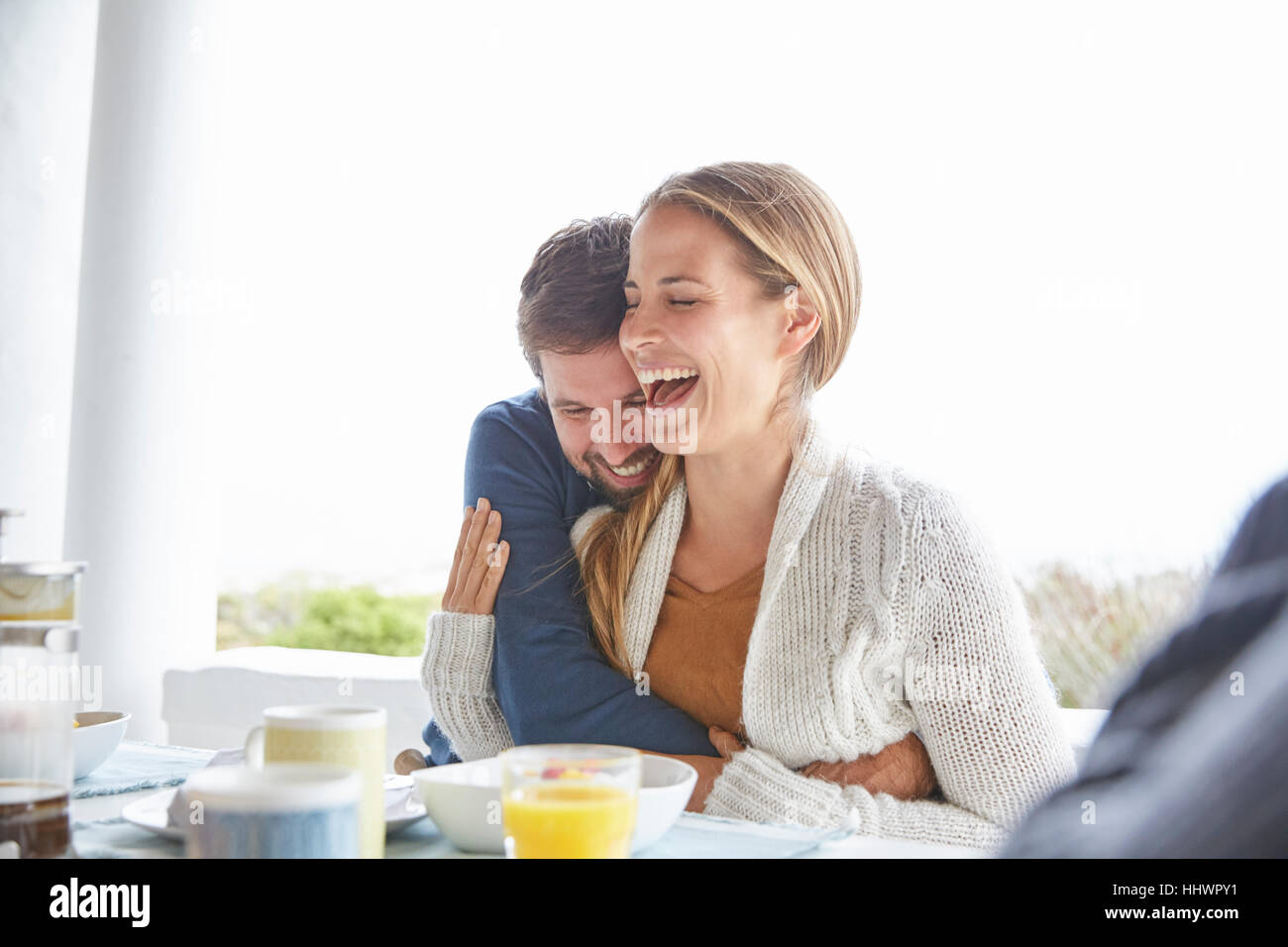 Affectionate couple hugging and laughing at breakfast on patio Stock ...