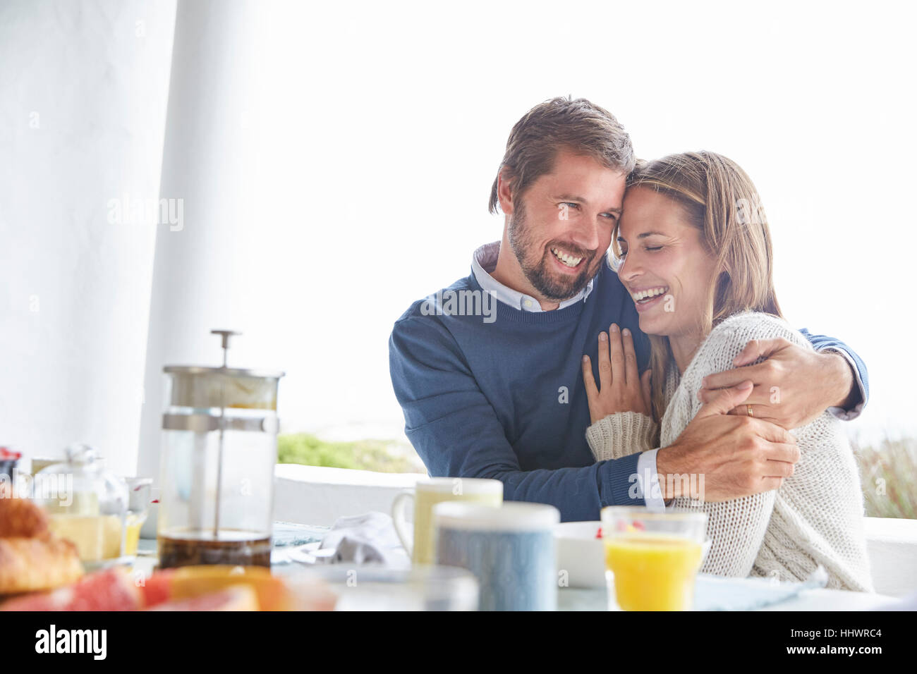 Smiling affectionate couple hugging at patio breakfast table Stock ...