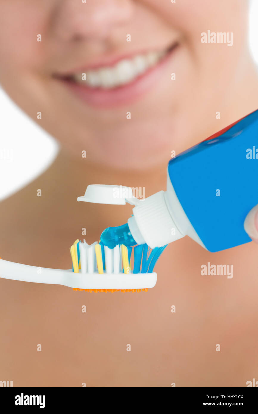 Smiling woman putting toothpaste on toothbrush on white background ...
