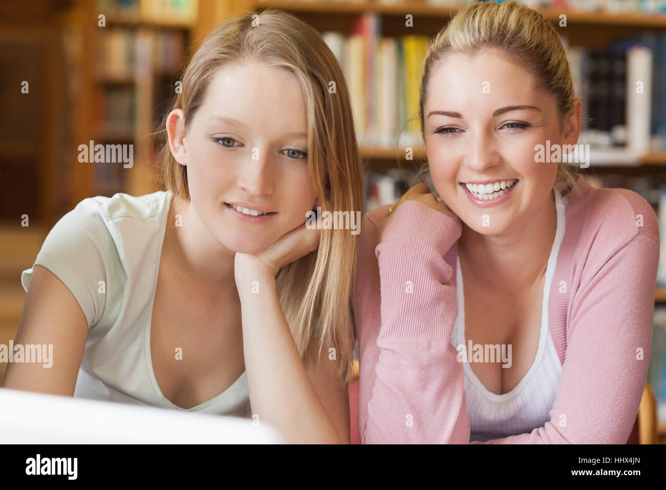 Friends sitting in library while smiling with laptop Stock Photo - Alamy