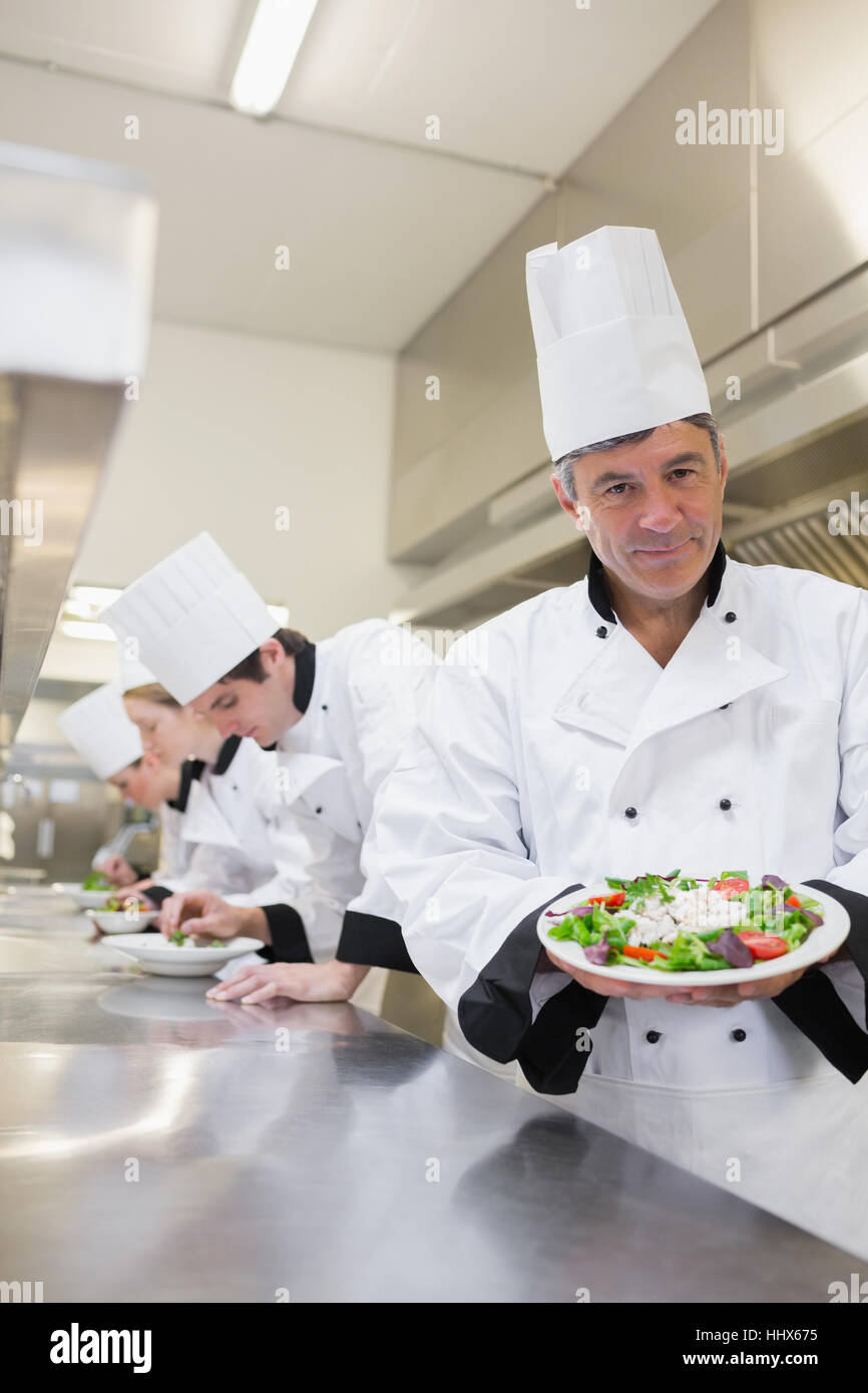 Cheerful chef showing his salad with workers in background in the ...