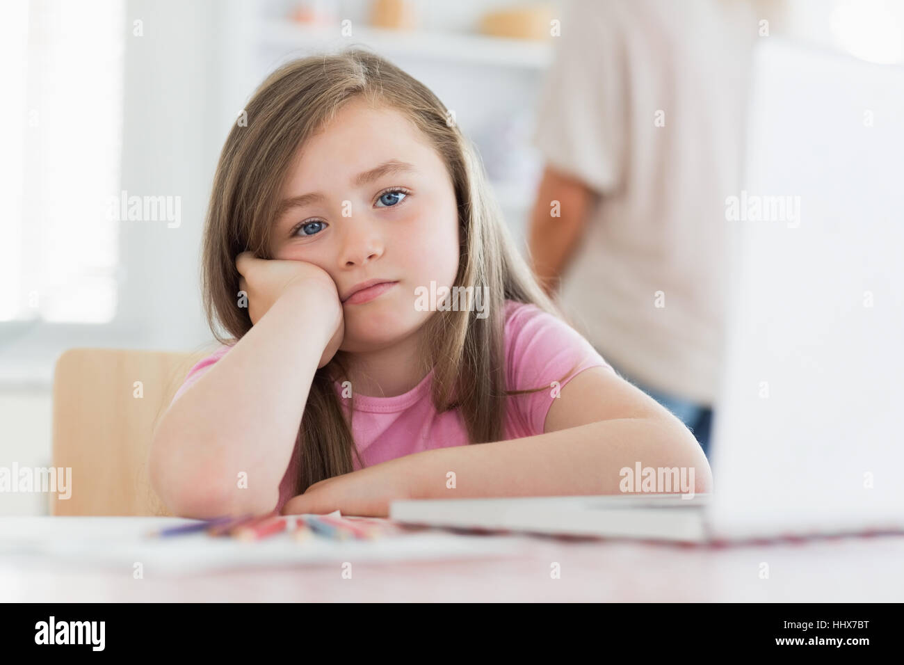 Child sitting while looking bored at the table at the kitchen with ...