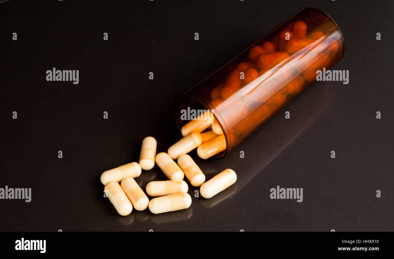 Tablets falling out of medicine jar on black background Stock Photo - Alamy
