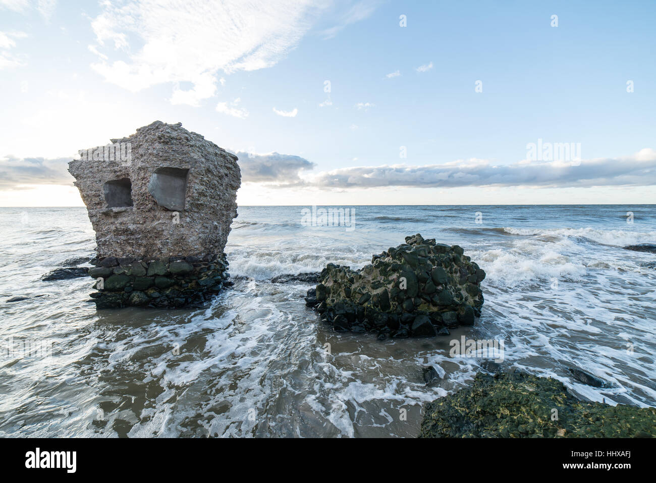 waves crushing over rocks and ruins of old fort at sunset on the beach ...