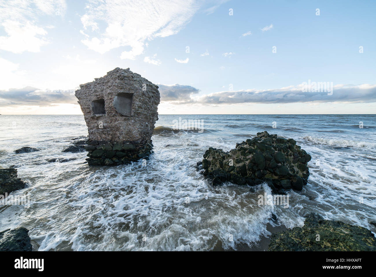 waves crushing over rocks and ruins of old fort at sunset on the beach ...