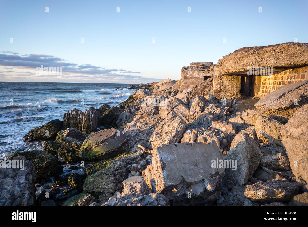 waves crushing over rocks and ruins of old fort at sunset on the beach ...