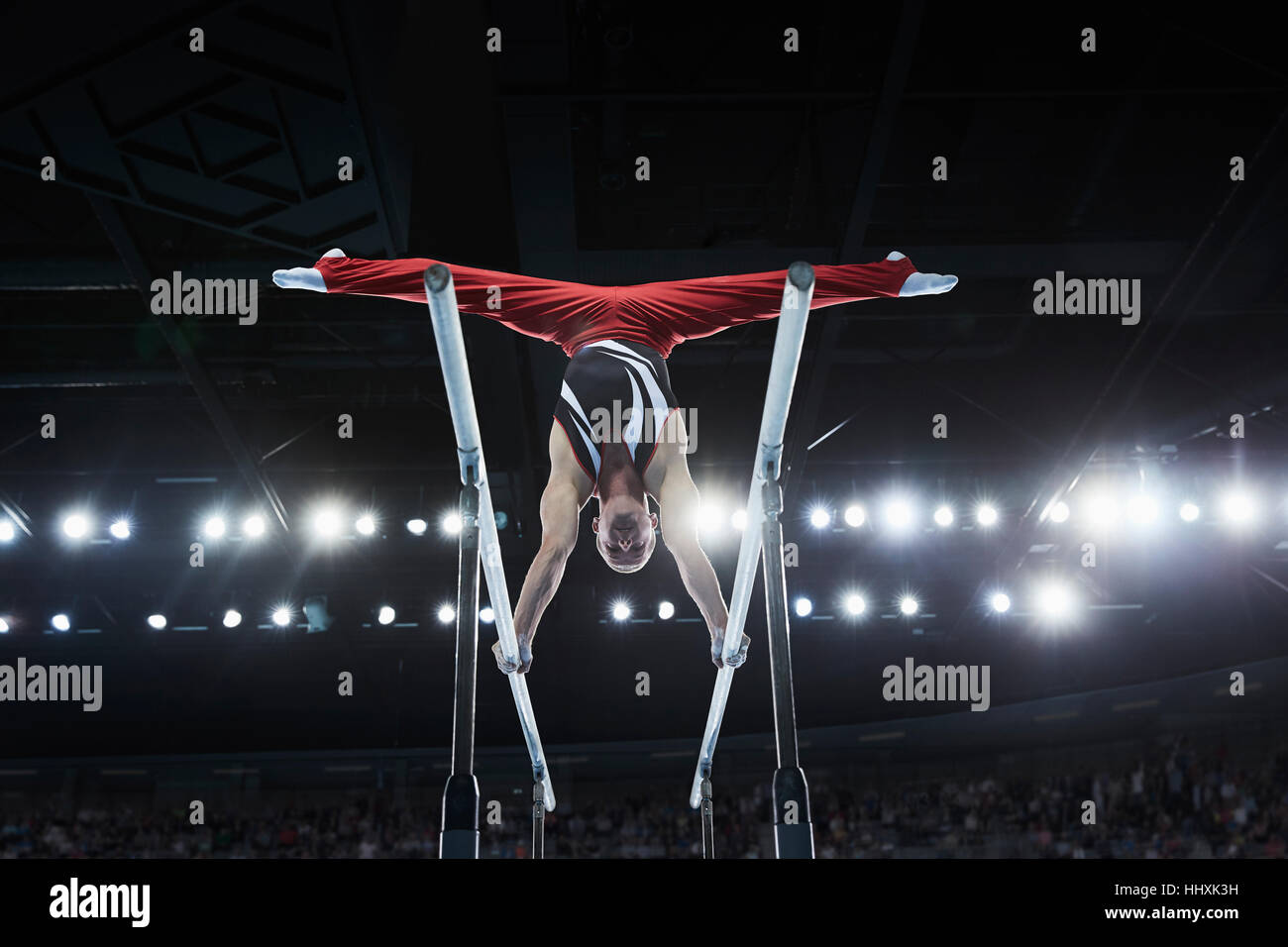 Male gymnast performing upside-down splits on parallel bars in arena ...