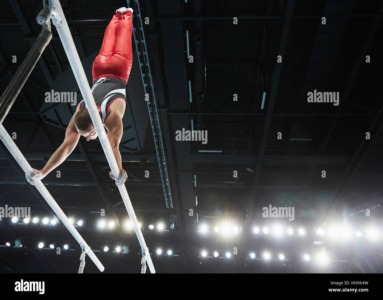 Male gymnast performing upside-down handstand on parallel bars in arena ...