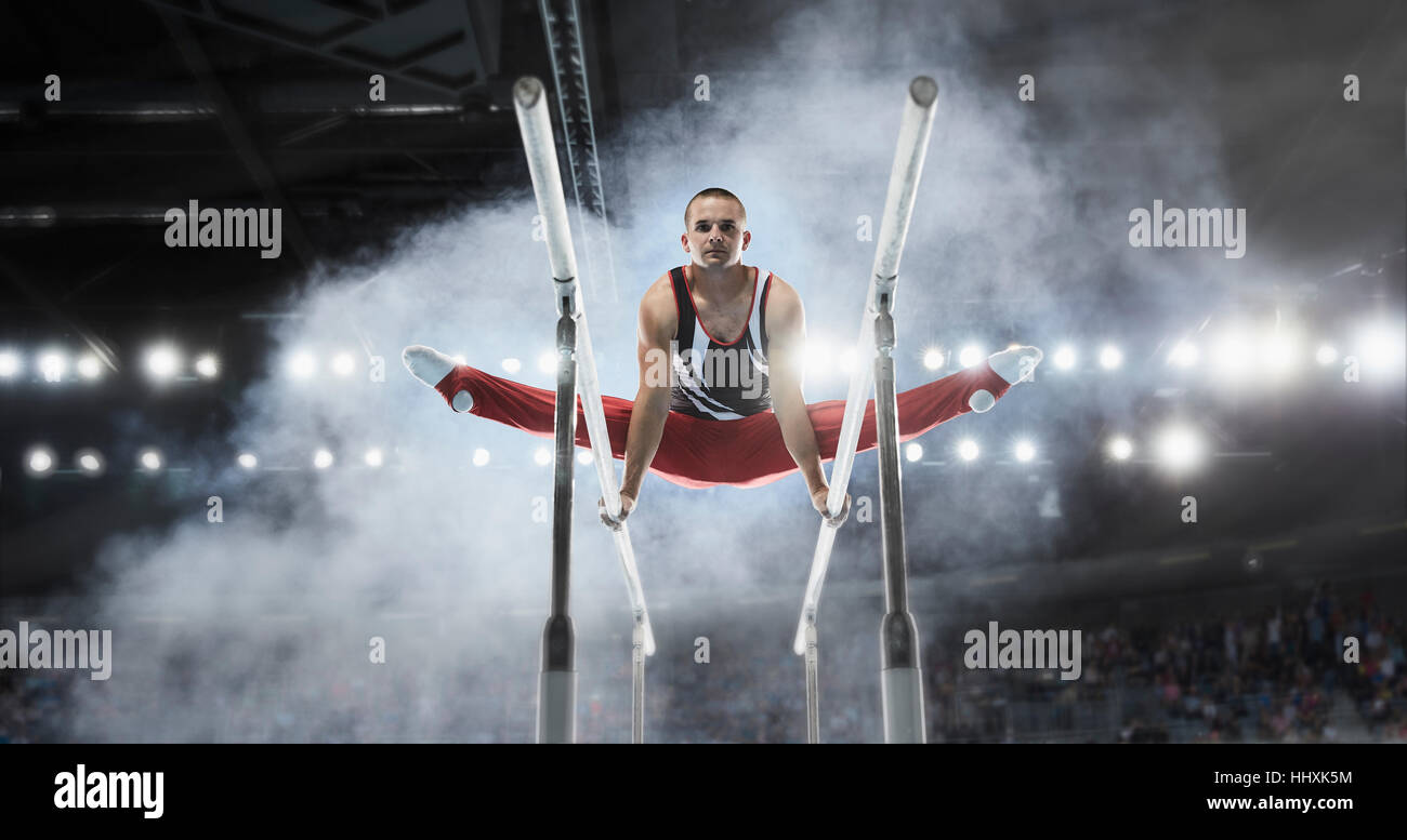 Focused male gymnast performing splits on parallel bars in arena Stock ...