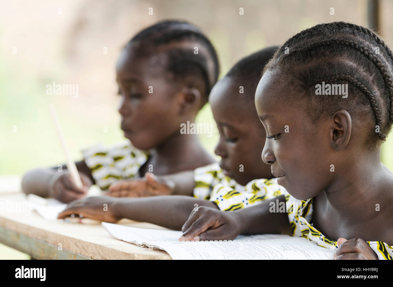 Two beautiful African girls and one African boy reading and writing at ...