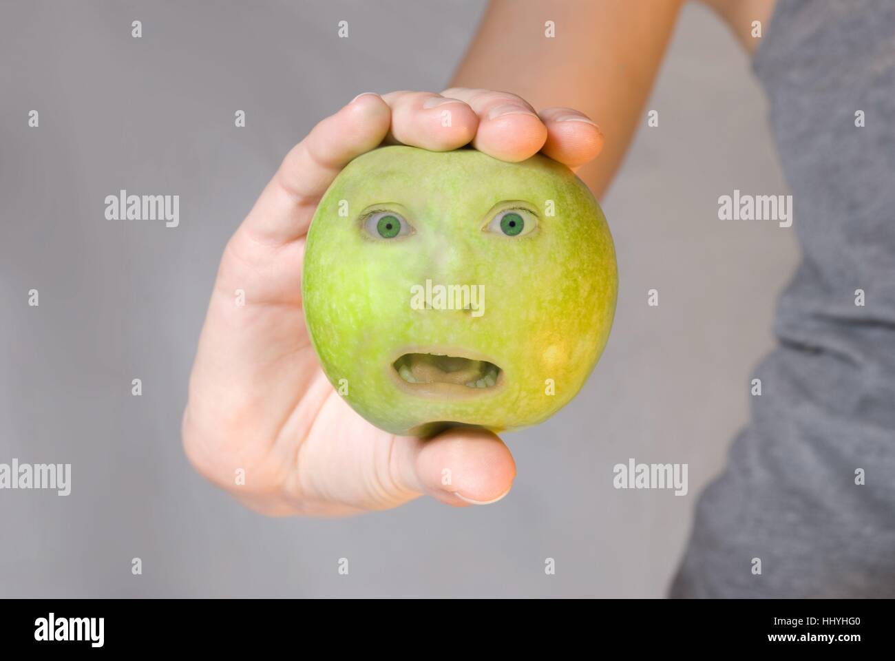 hands holds an green apple with a fearful looking face on it Stock ...