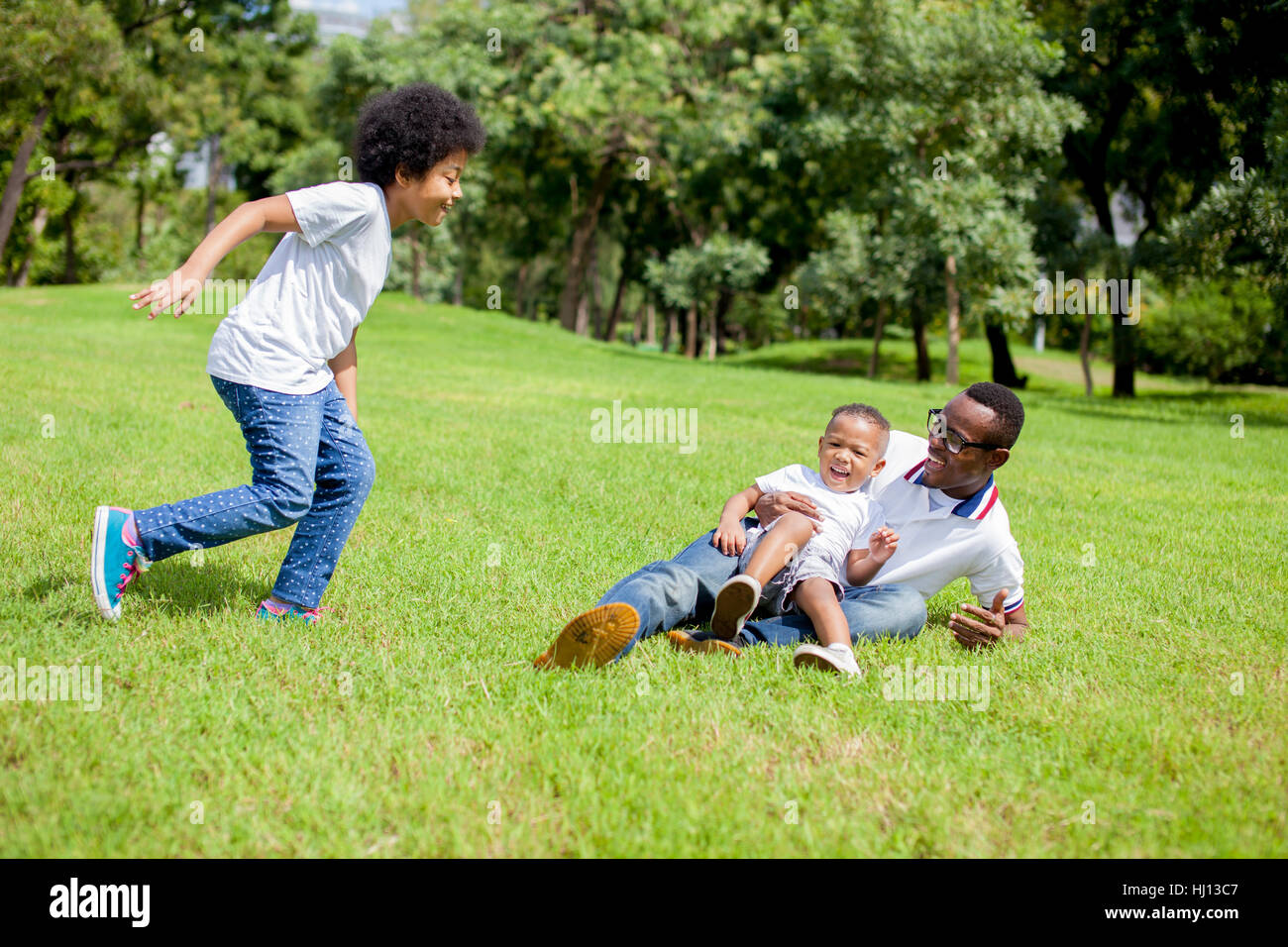 Two kids chasing and playing together while dad caught a boy in park ...