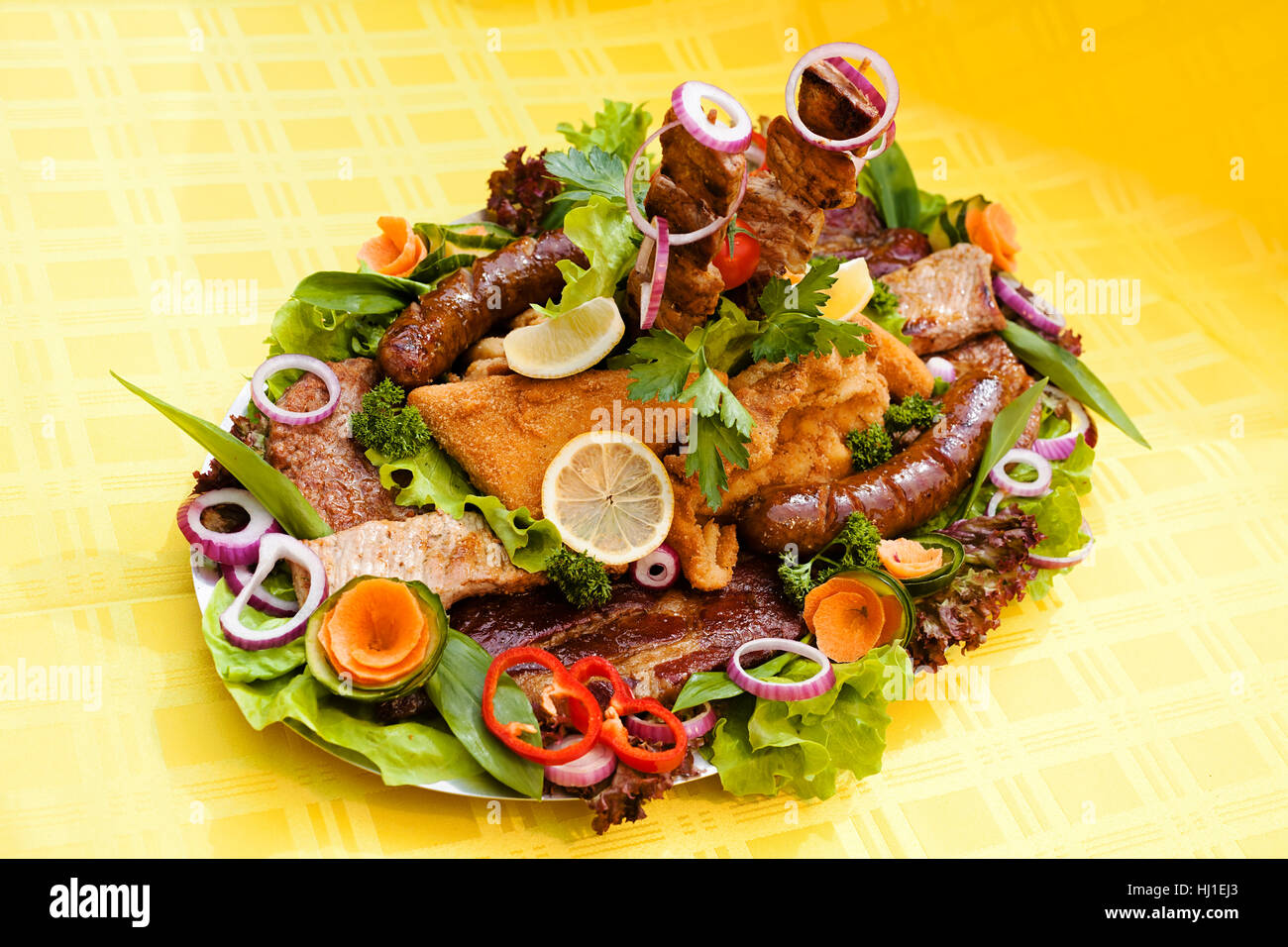 mixed meat decorated with lots of vegetables on oval on the yellow ...