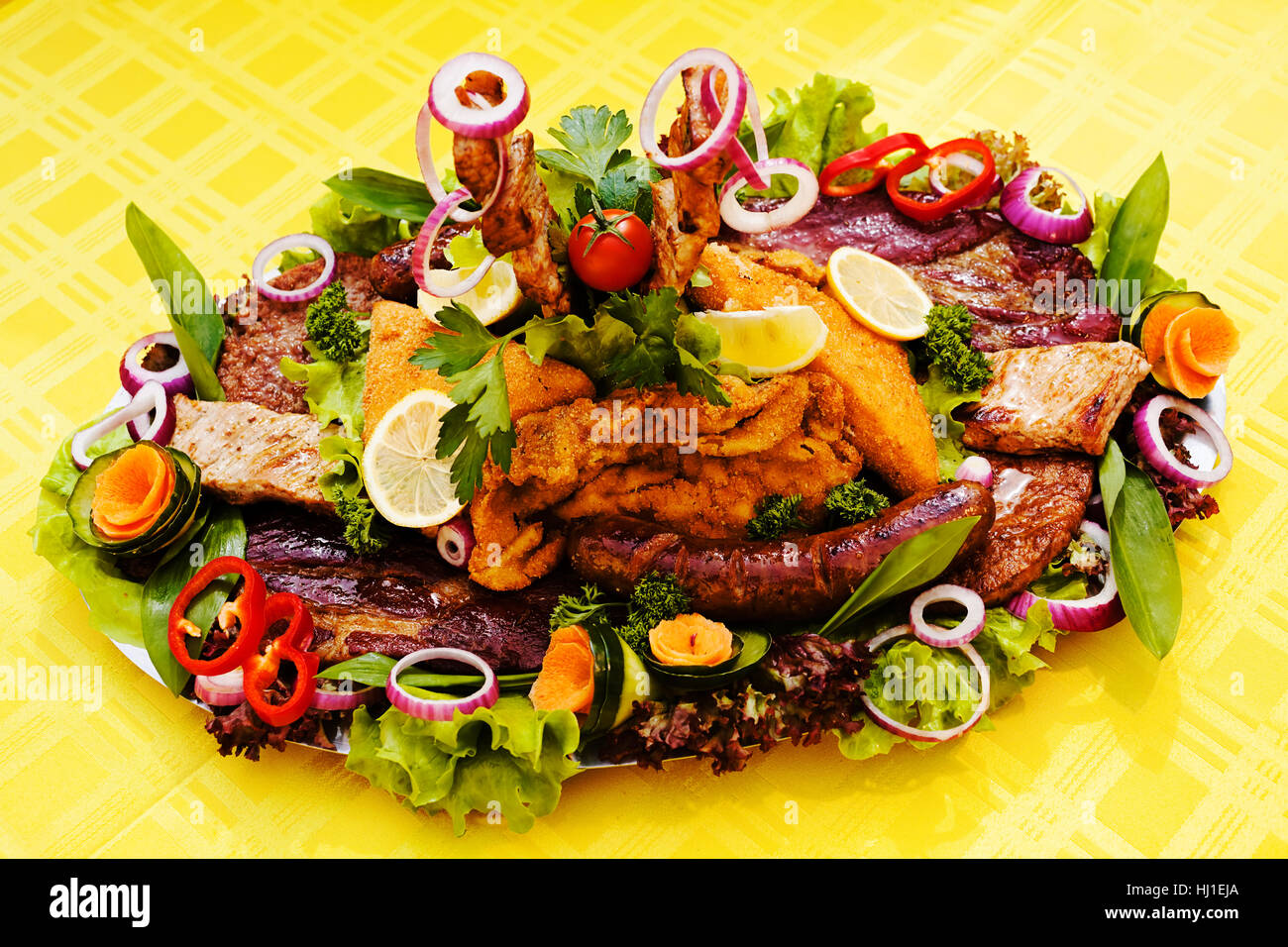 mixed meat decorated with lots of vegetables on oval on the yellow ...