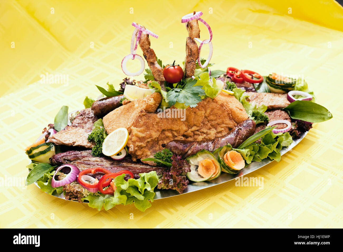 mixed meat decorated with lots of vegetables on oval on the yellow ...