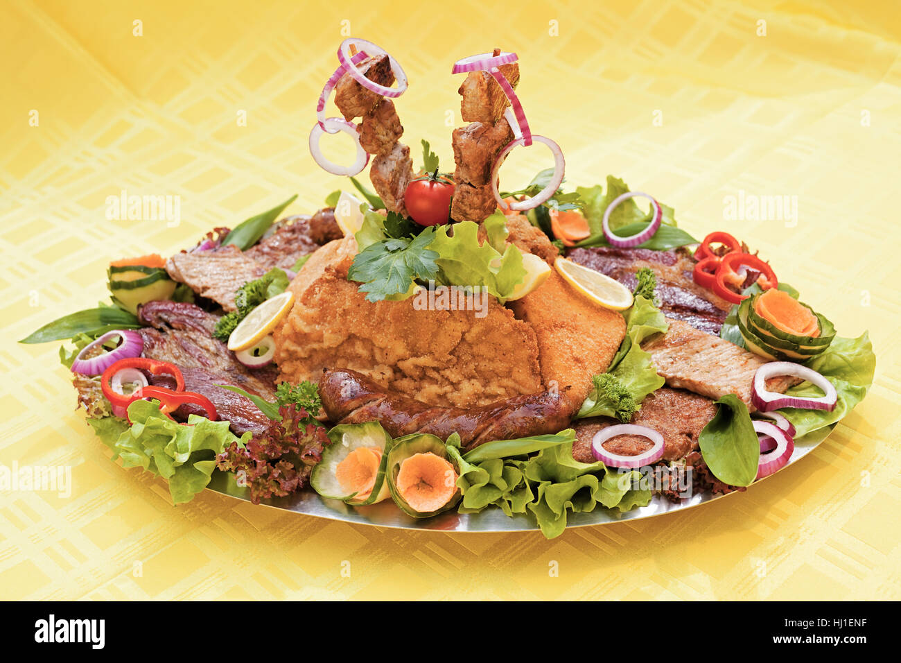 mixed meat decorated with lots of vegetables on oval on the yellow ...