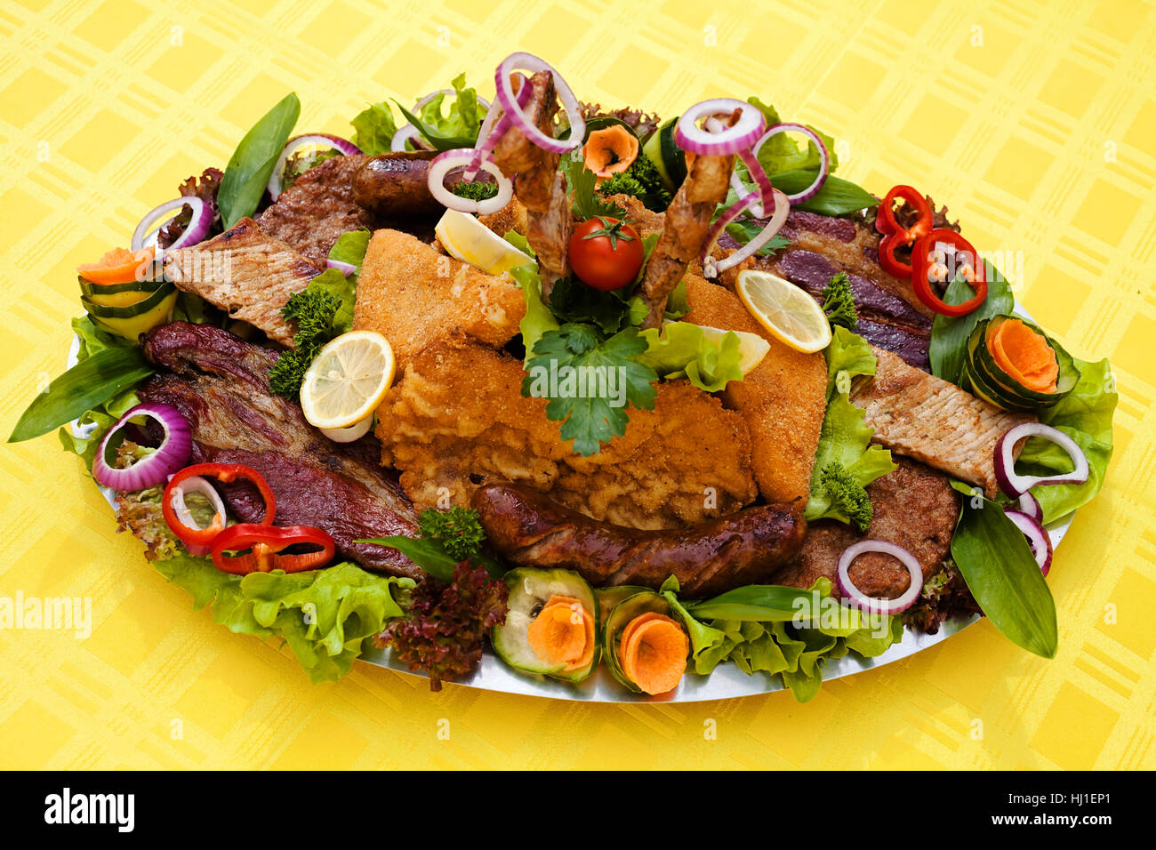 mixed meat decorated with lots of vegetables on oval on the yellow ...