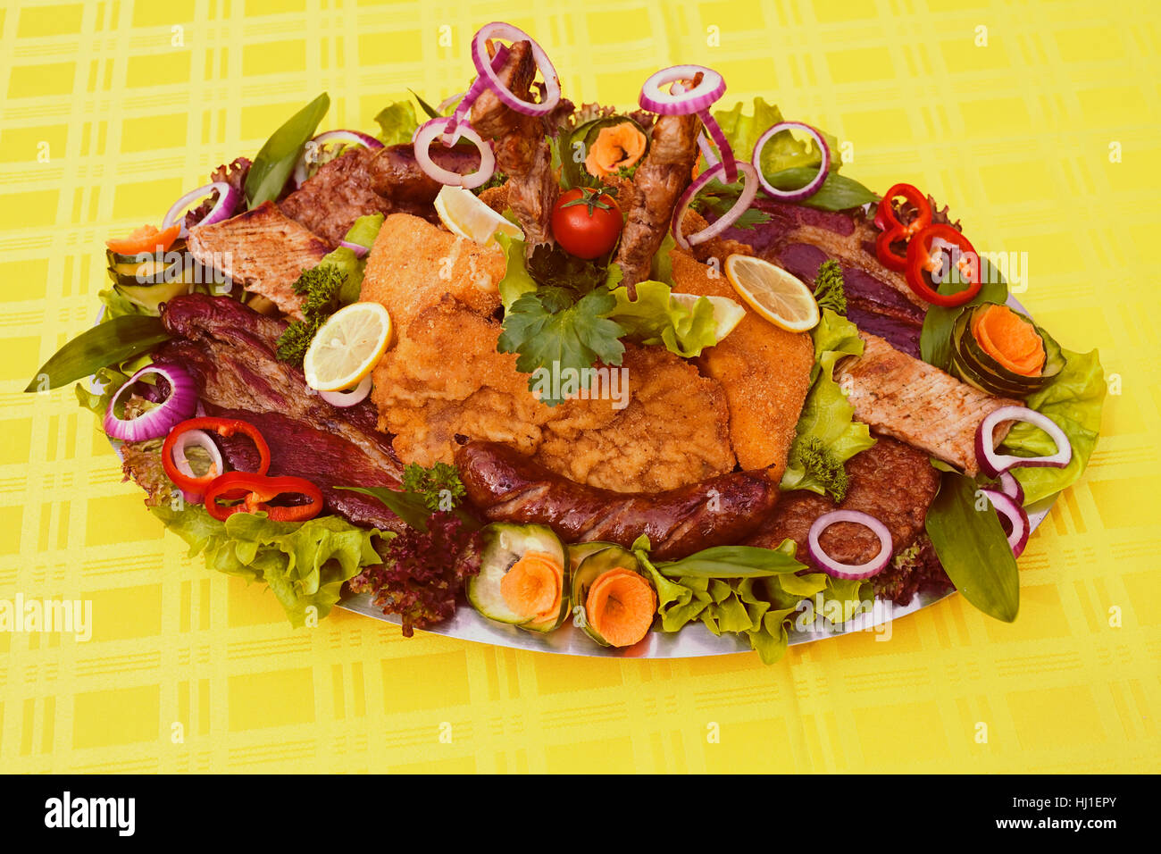 mixed meat decorated with lots of vegetables on oval on the yellow ...