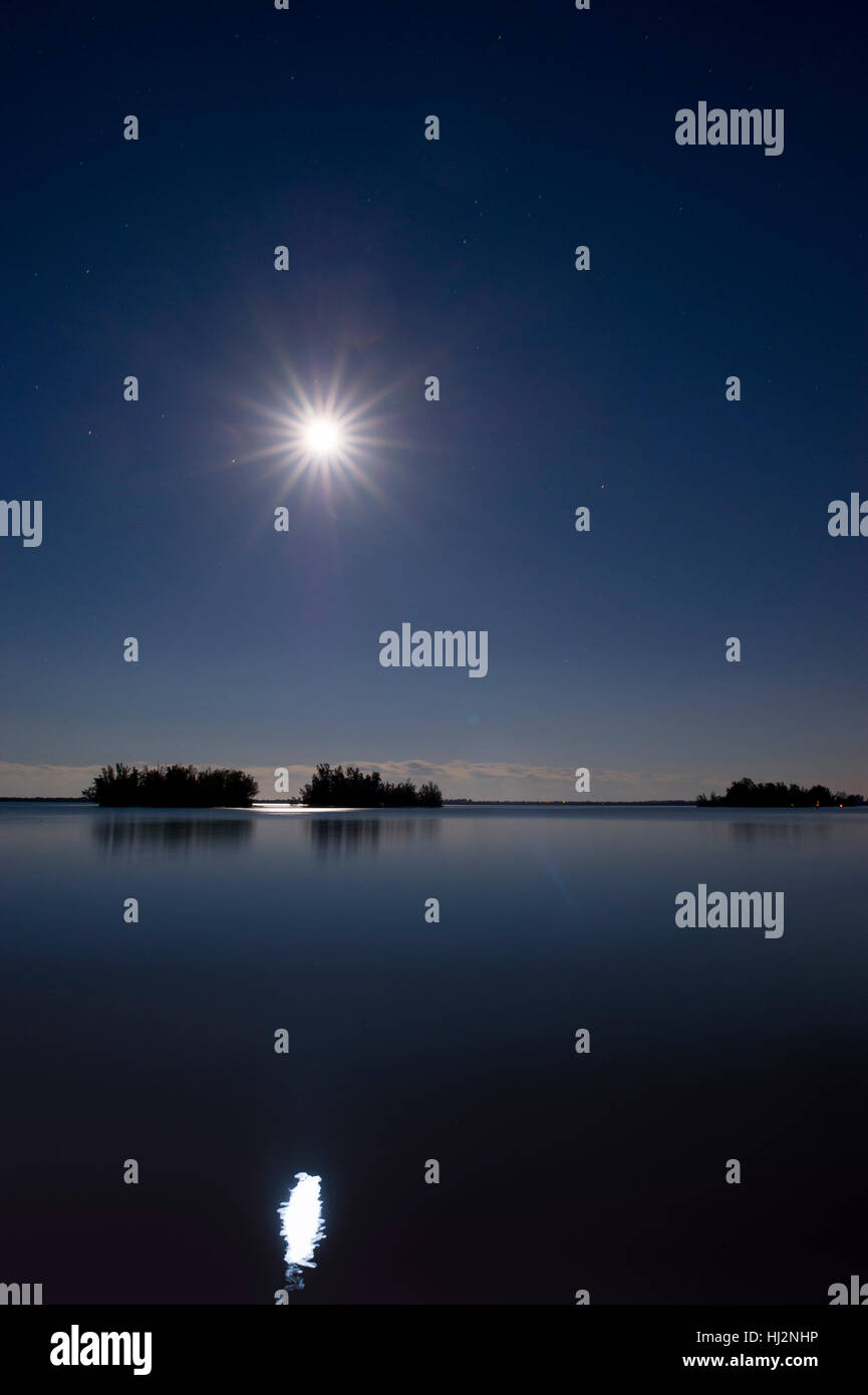 A nightscape of a calm river with a bright moon over some small islands ...
