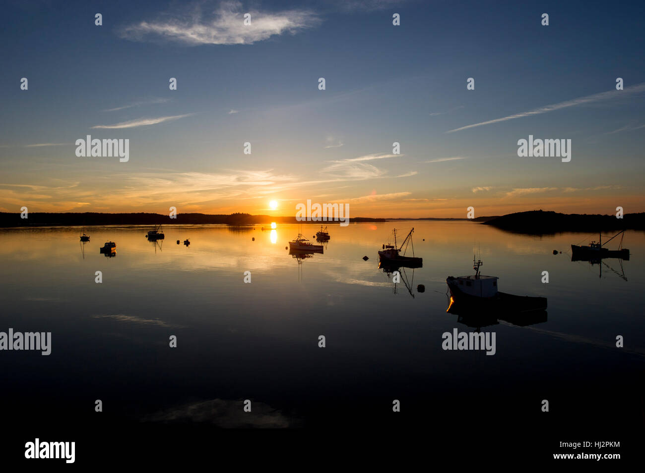 The sun sets over a calm harbor with many fishing boats anchored Stock ...