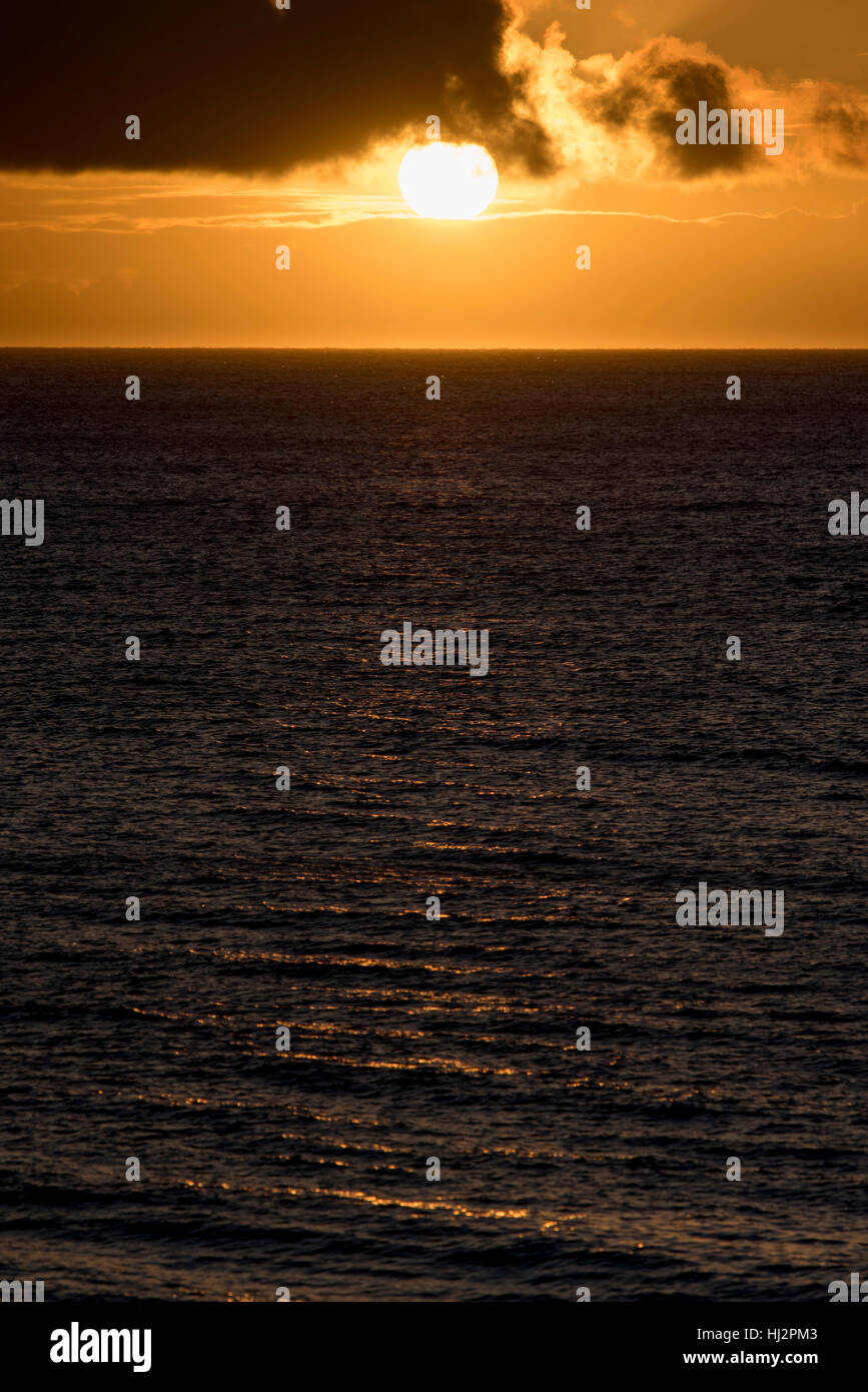 A bright yellow sun setting over the ocean Stock Photo - Alamy