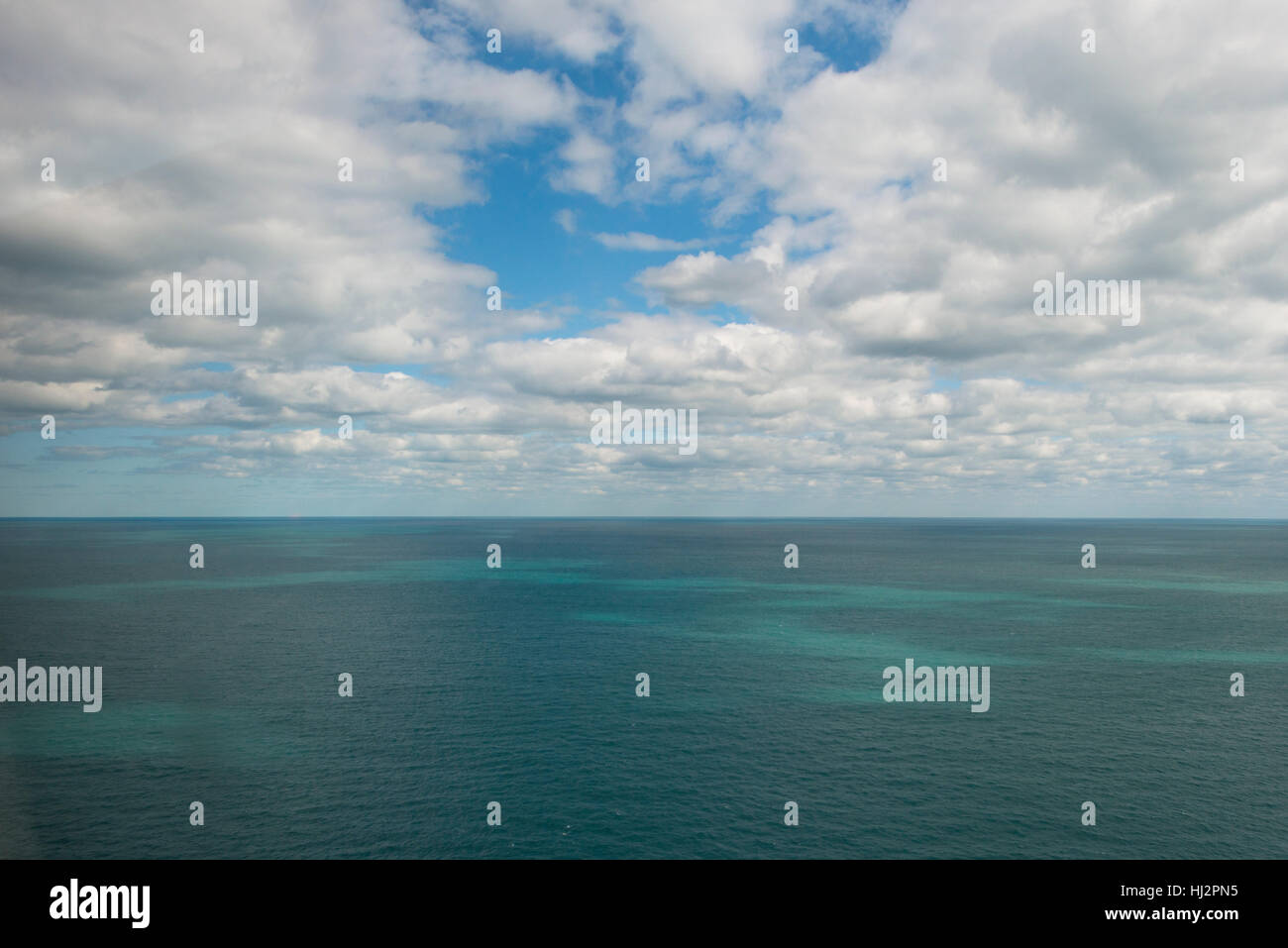 Aerial photo of a turquoise ocean with puffy white clouds and a blue ...