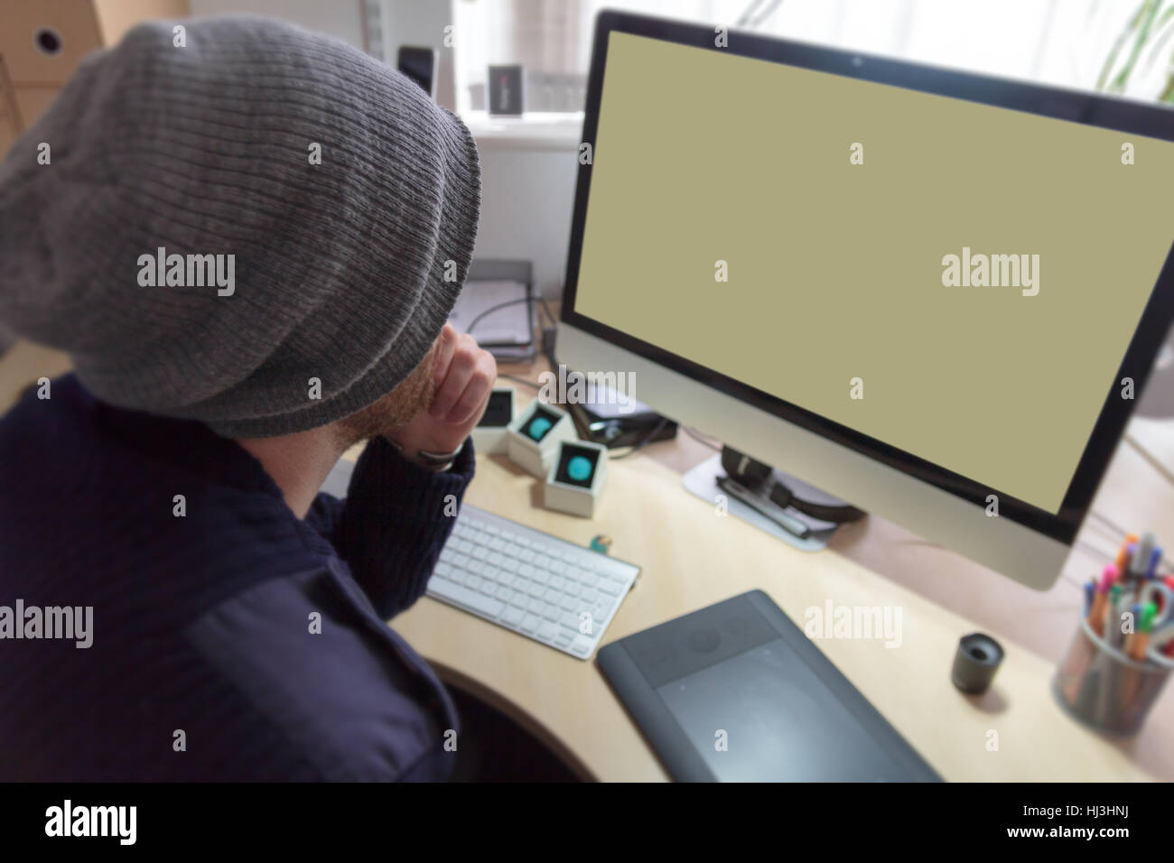 Creative man sat at desk working on designs on a computer using a ...