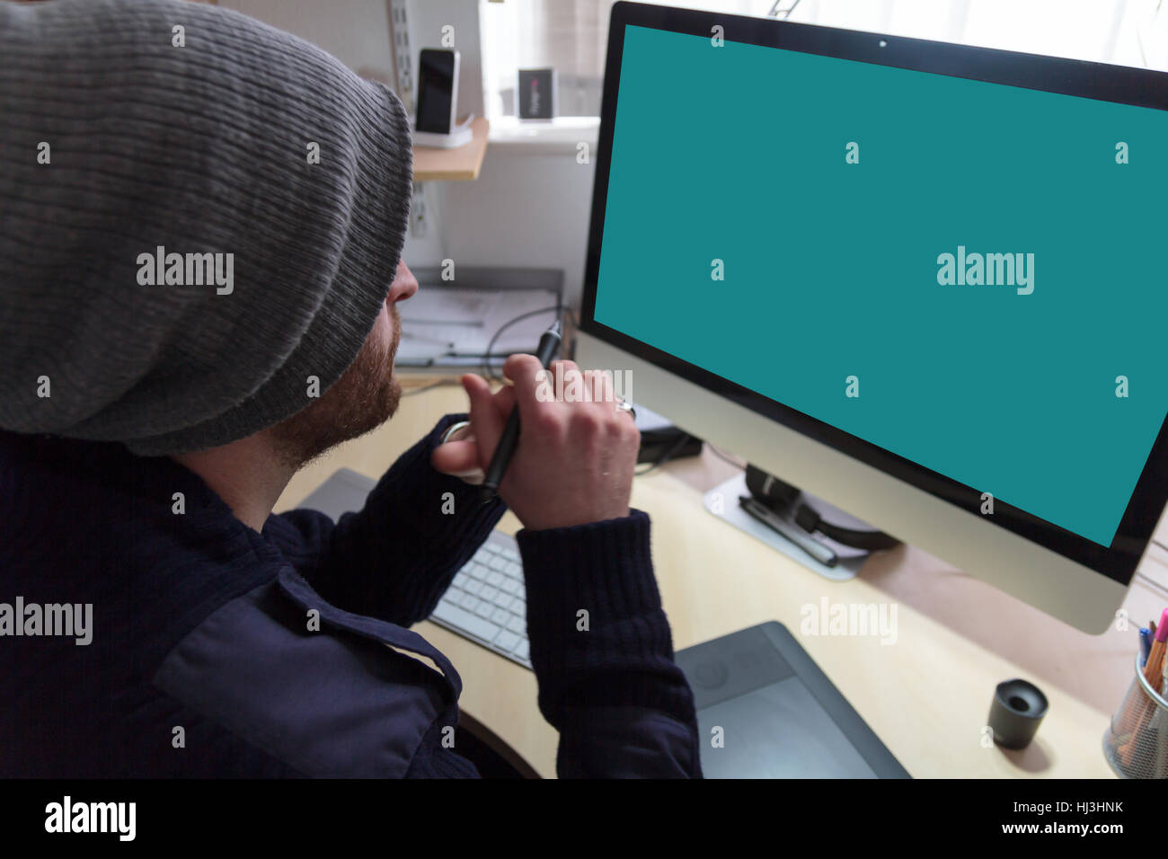 Creative man sat at desk working on designs on a computer using a ...