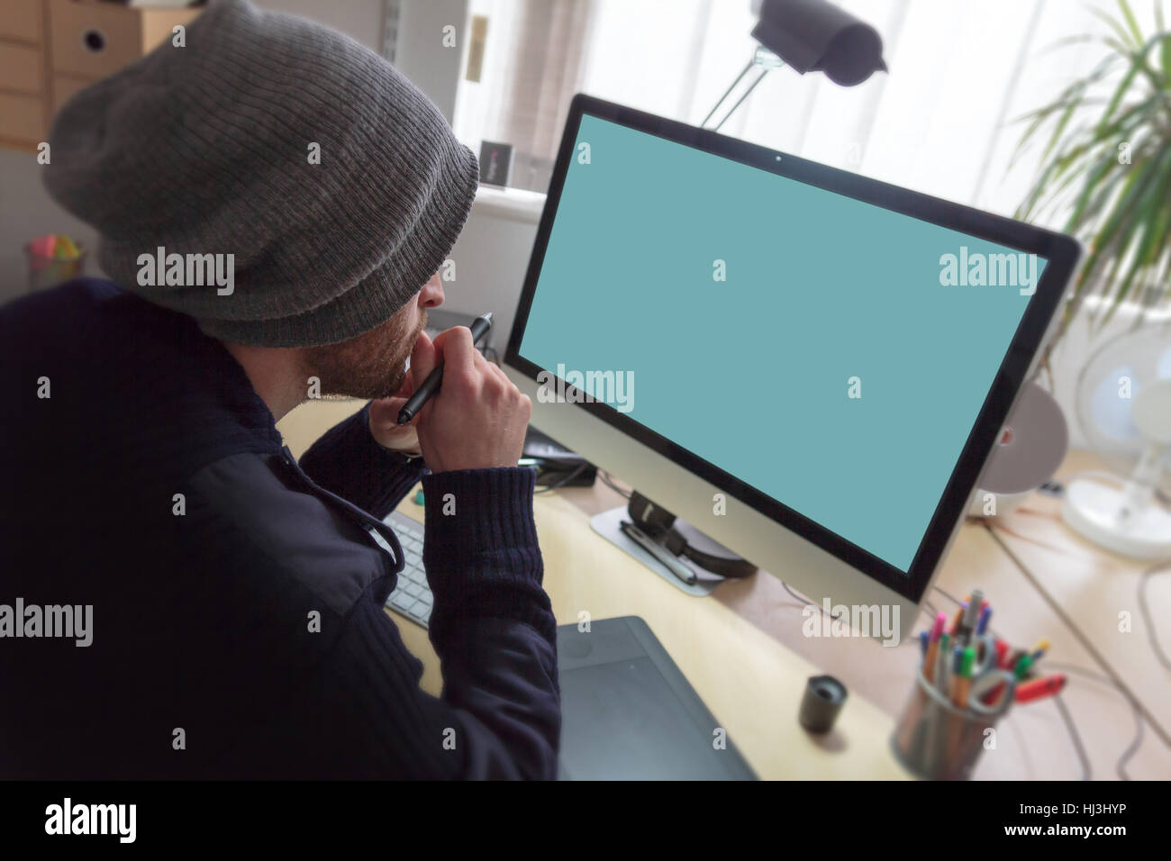 Creative man sat at desk working on designs on a computer using a ...