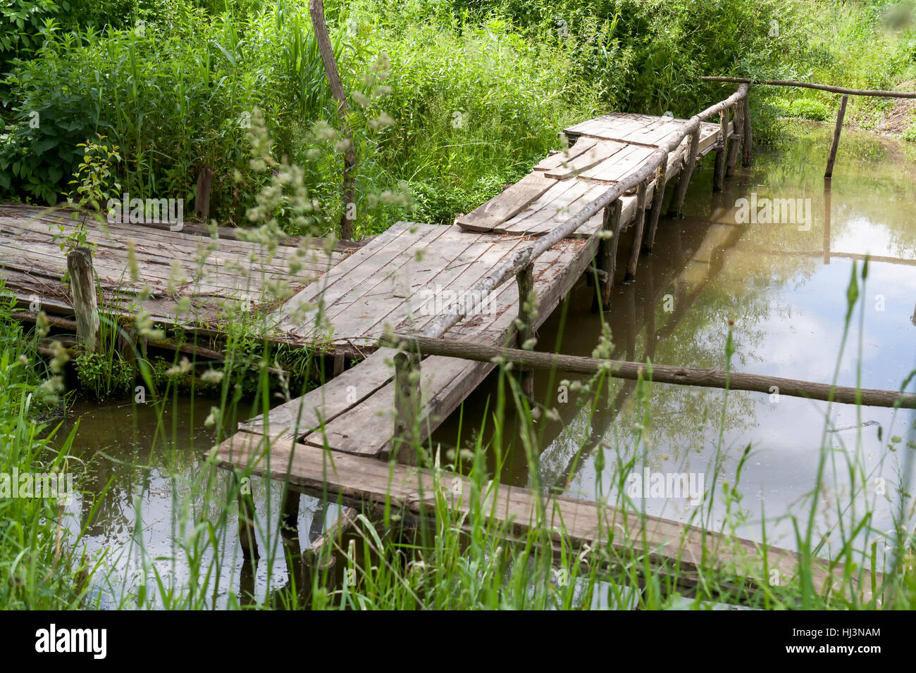 Old wooden bridge over the lake overgrown with grass. Old rural ...