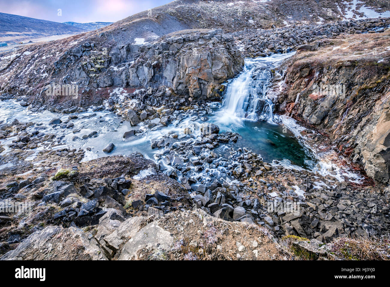 A waterfall in Iceland cascades down the side of a rugged mountain into ...
