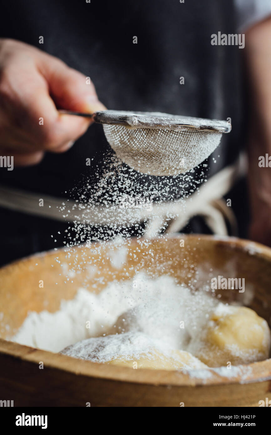 Person adds flour to a pastry through the strainer. Vertical studio ...