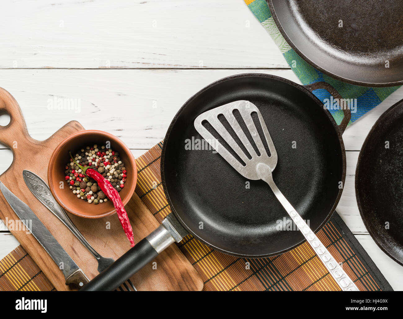 Several empty cast-iron frying pans on a white wooden background. View ...