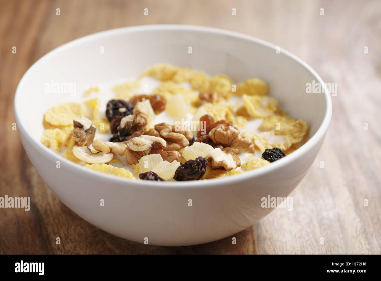 closeup photo of corn flakes with fruits and nuts in white bowl on wood ...