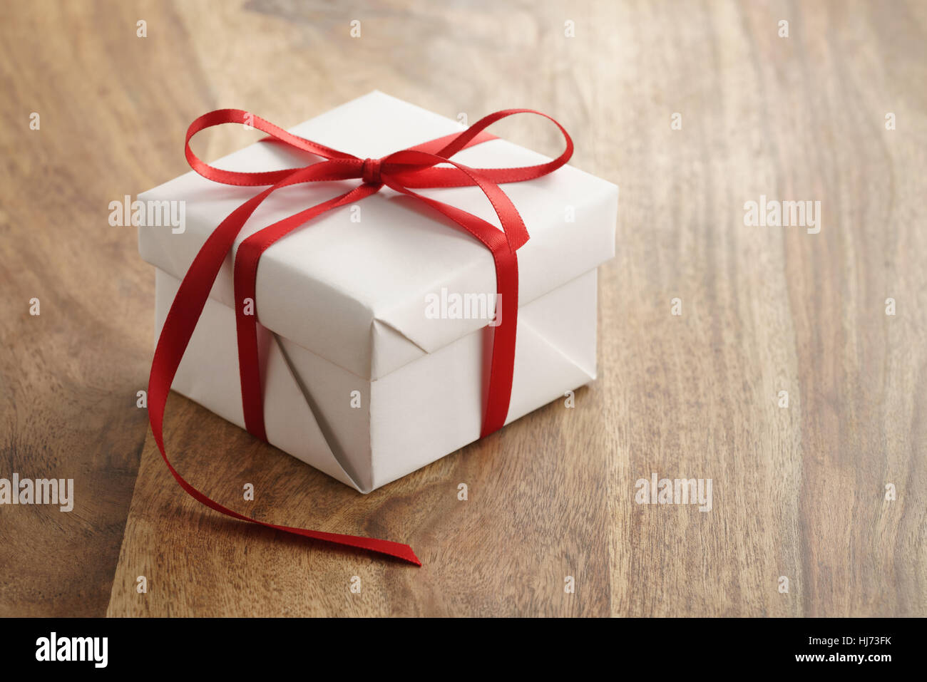 white paper gift box with thin red ribbon bow on old wood table Stock ...