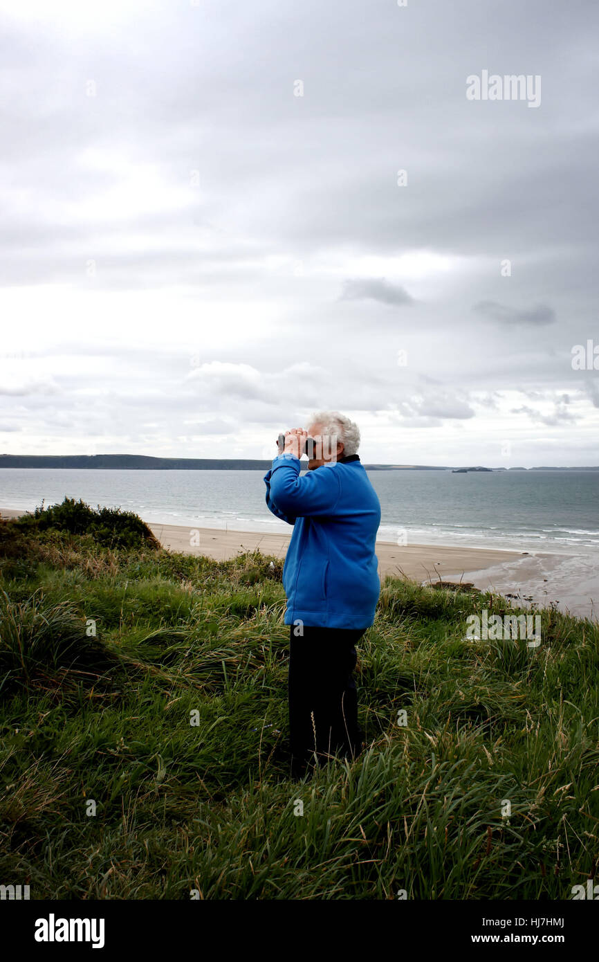 A senior lady looking through binoculars on the coastal path Stock ...